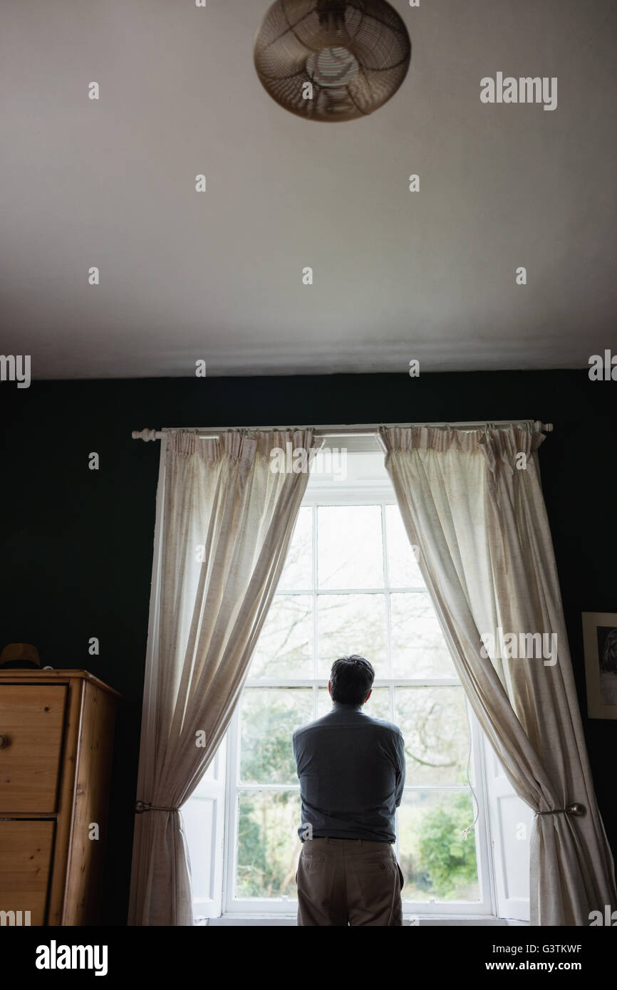 Rear view of mature man looking through window Stock Photo - Alamy
