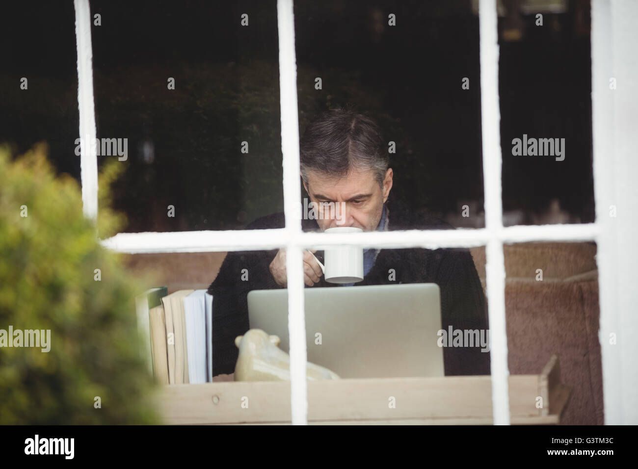 Mature man drinking cup of tea while working at desk Stock Photo - Alamy