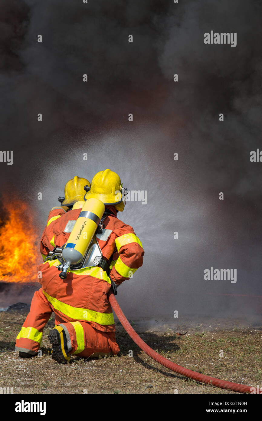 2 firemen spraying water in fire fighting with fire and dark smoke ...