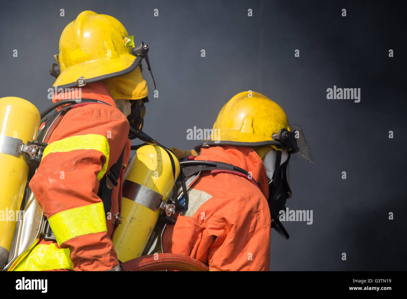 2 firefighters in operation and dark smoke background Stock Photo - Alamy