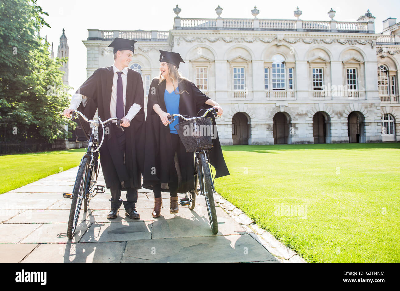 Two young students in graduation gowns pushing bicycles through the ...