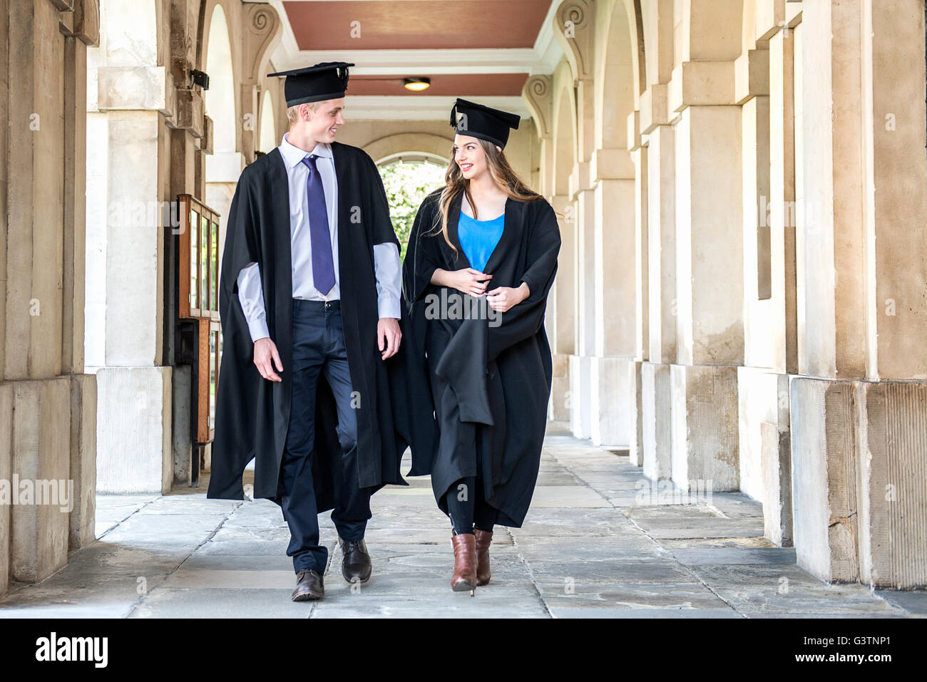 Two students in graduation gowns walking outside a building at ...