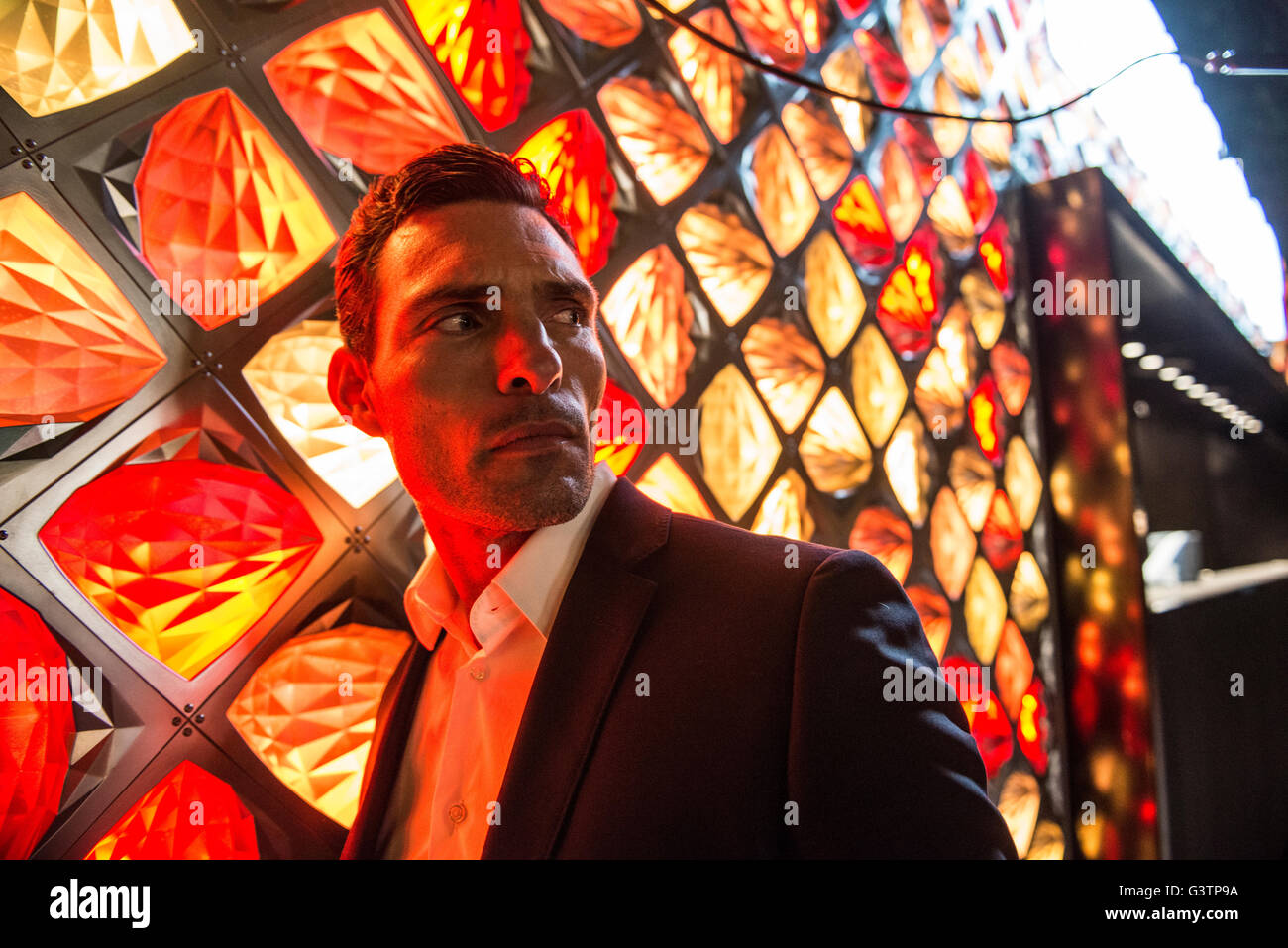 A smartly dressed man bathed in red light in front of a light fixture ...