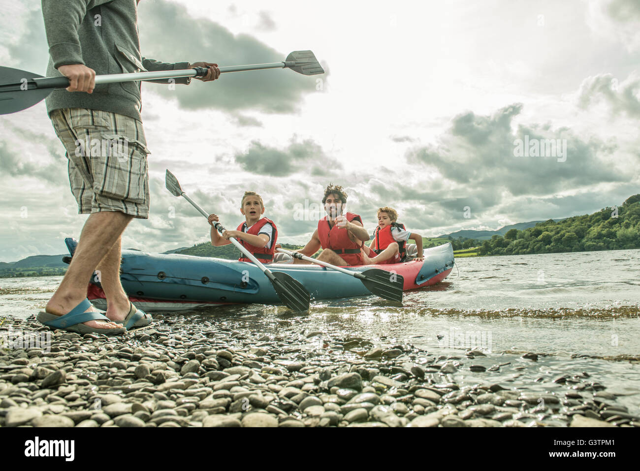 A man handing a paddle to people in a kayak on the water of Bala Lake ...