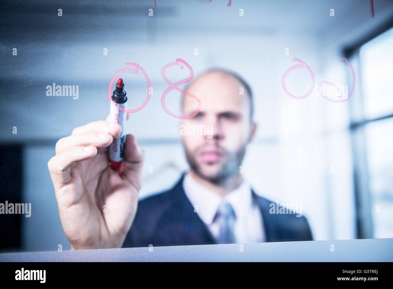 A professional man writing numbers on glass in an office environment ...