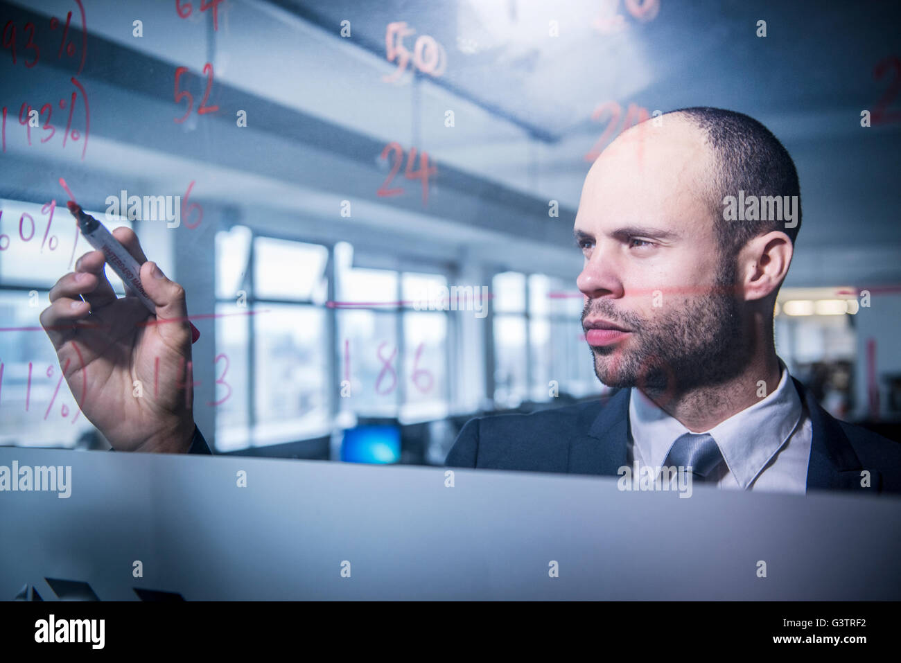 A professional man writing numbers on glass in an office environment ...