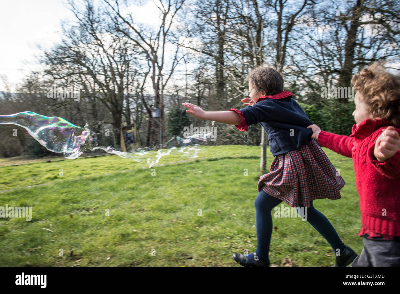 Two young children chasing bubbles around a garden Stock Photo - Alamy