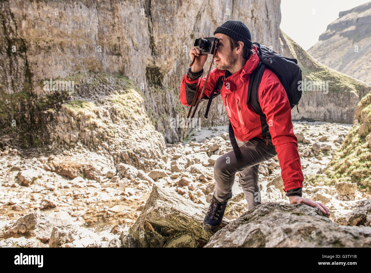A mountaineer climbing over rocks taking photographs in rugged terrain ...