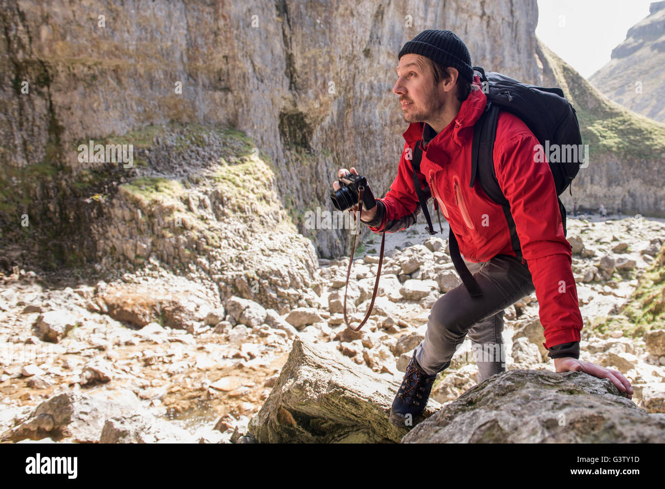 A mountaineer climbing over rocks taking photographs in rugged terrain ...