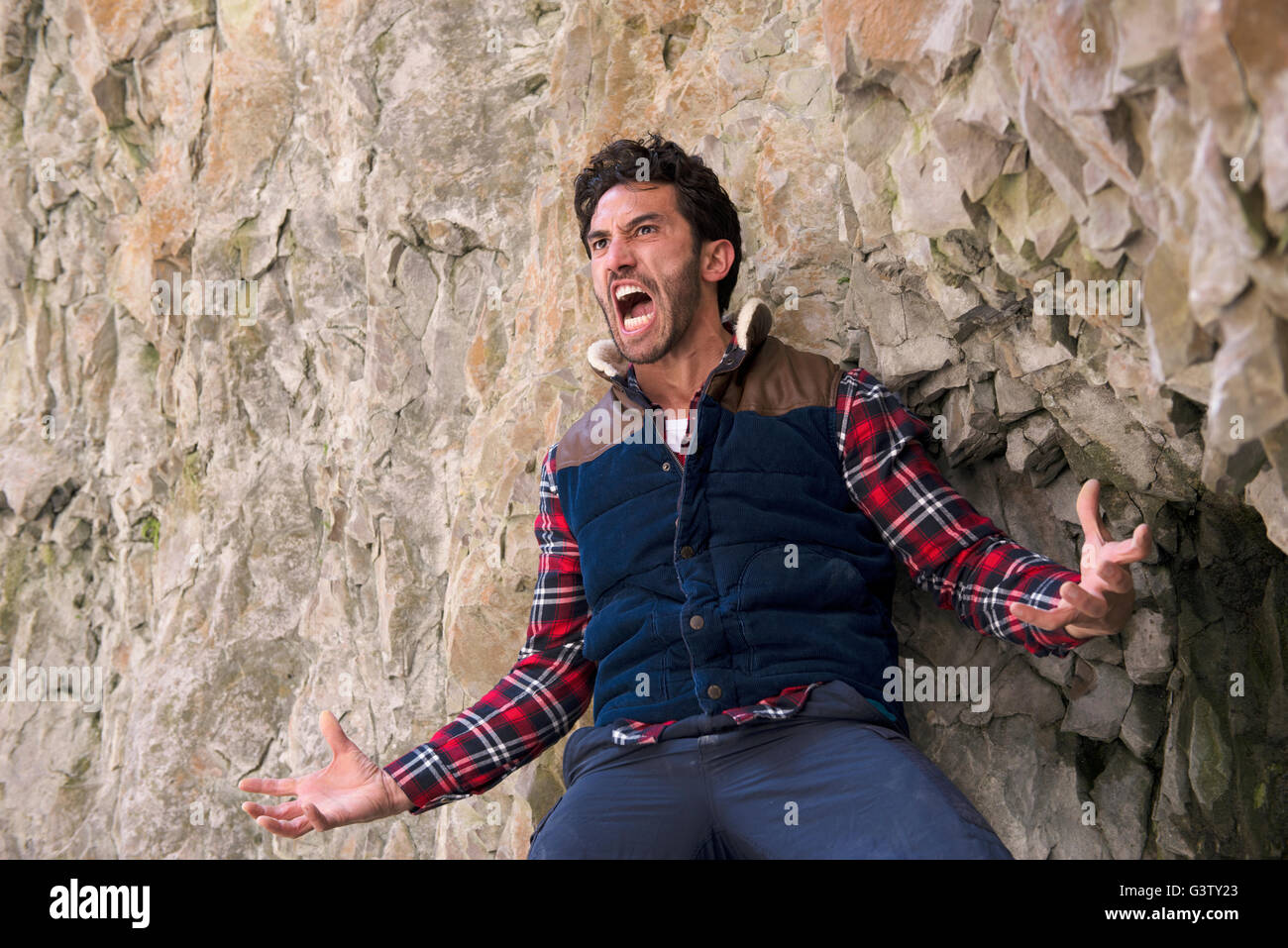 A climber with an angry expression standing on a ledge in rugged ...