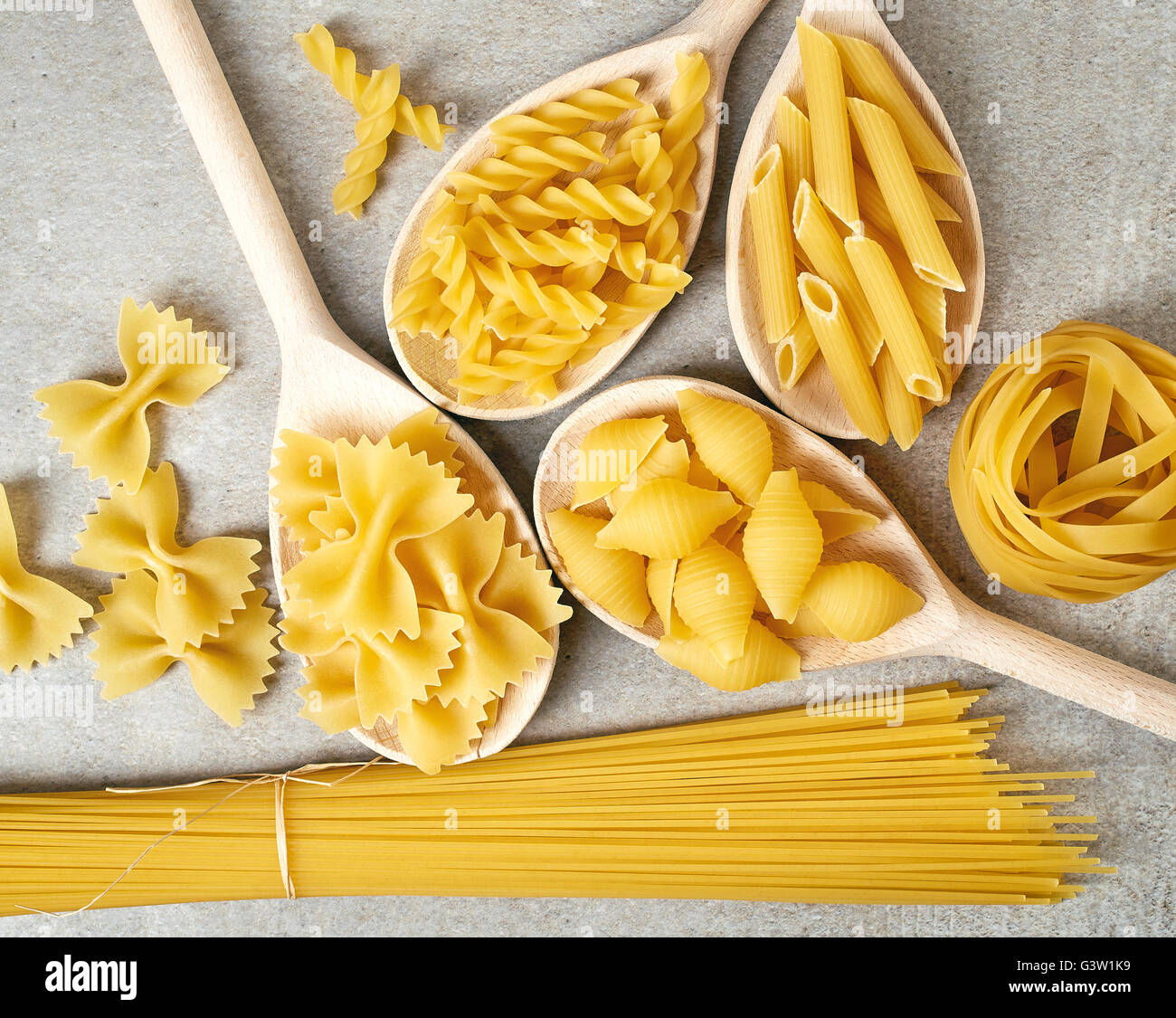 Various types of pasta in wooden spoons on stone table, top view Stock ...