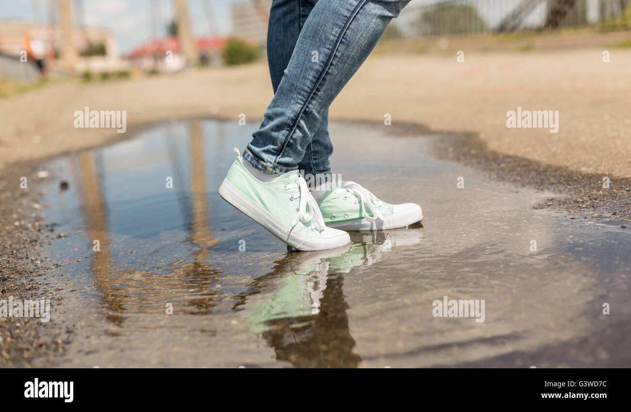 Woman in sport shoes standing in a puddle. Close up shot of foots in a ...