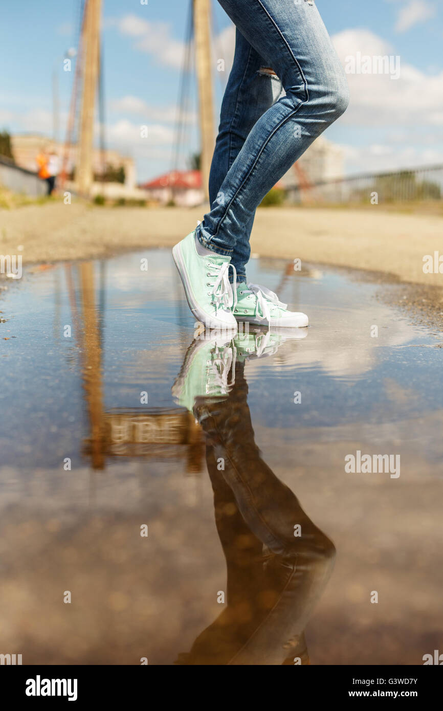 Woman in sport shoes standing in a puddle. Close up shot of foots in a ...