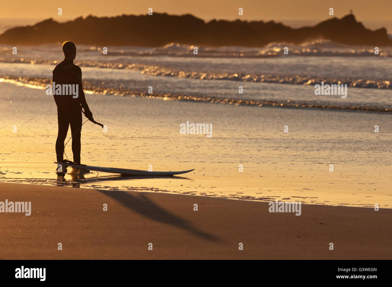Surfer at Sunset in silhouette casting long shadows on the sand ...