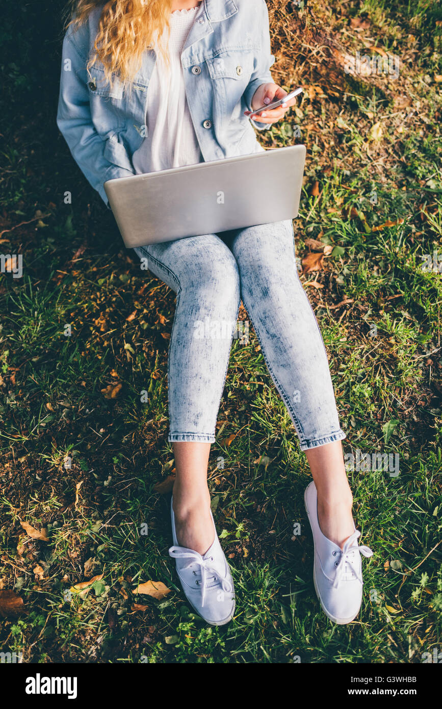 From the neck down view of young blonde woman sitting ont he grass ...