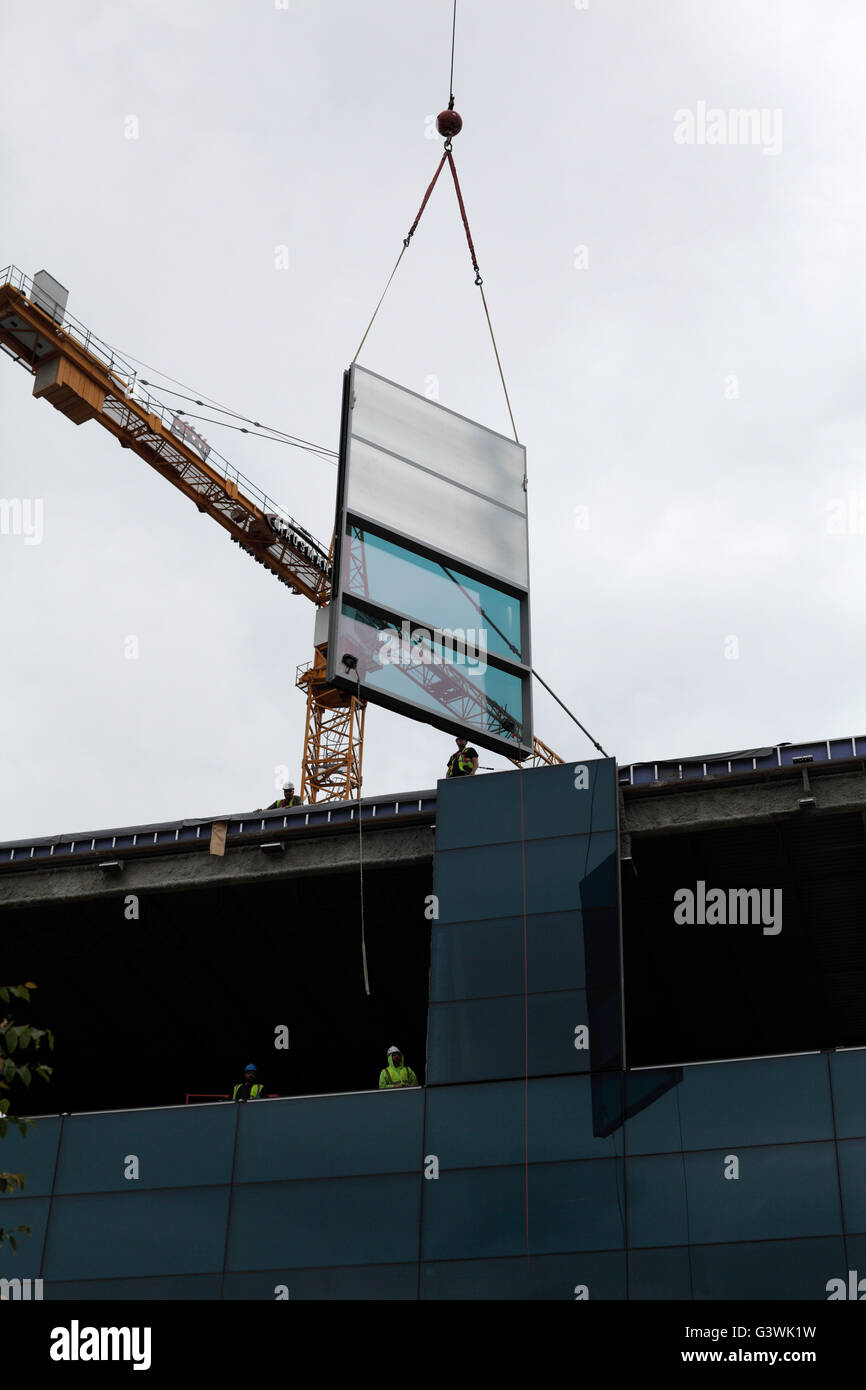 A construction crew prepares to attach a window panel to the side of a ...