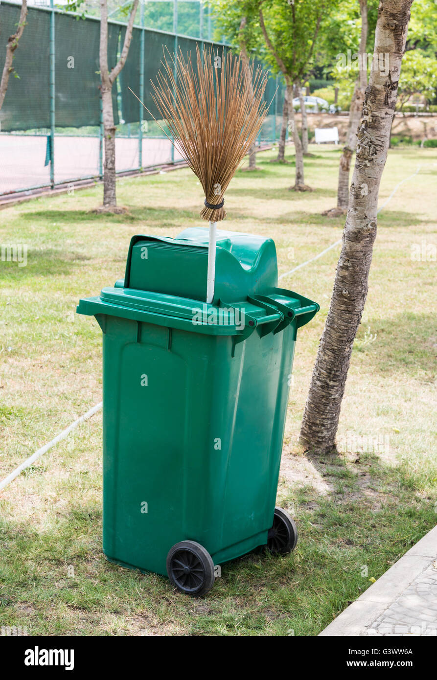 Green trash can and coconut stick broom on the field near the tennis ...