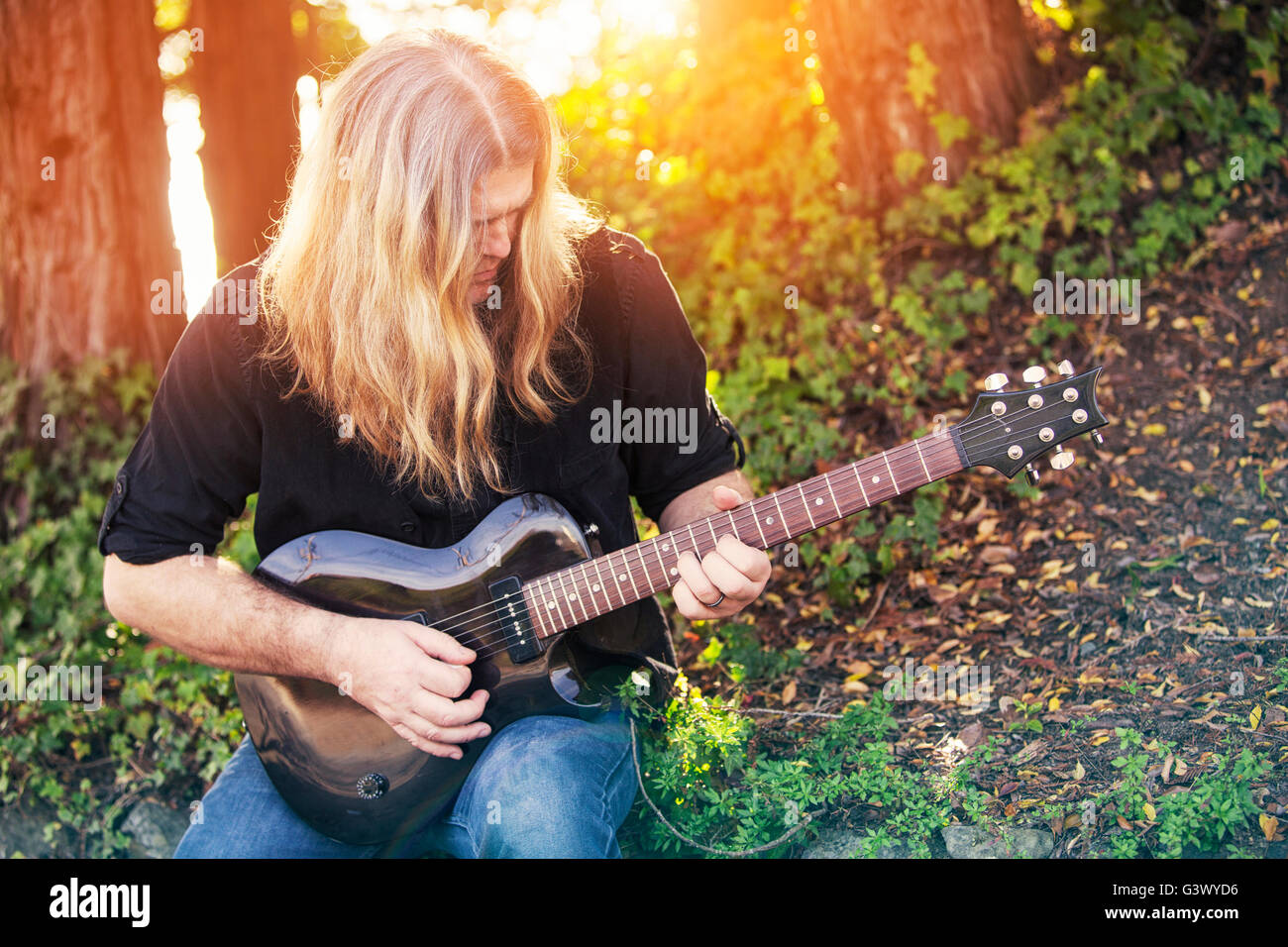 man with long hair sitting by trees and playing guitar Stock Photo - Alamy
