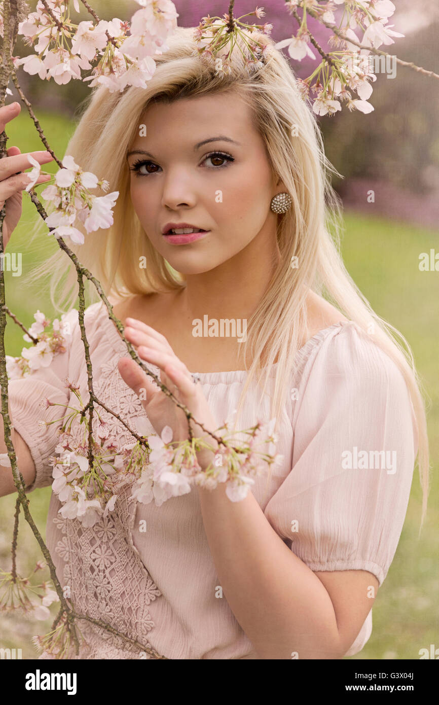 Portrait of a beautiful young woman posing under spring cherry blossoms ...