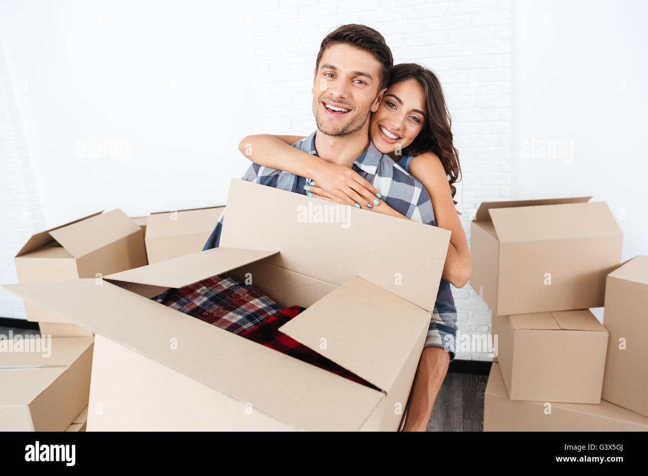 Smiling young couple carrying cardboard boxes and hugging in new flat ...