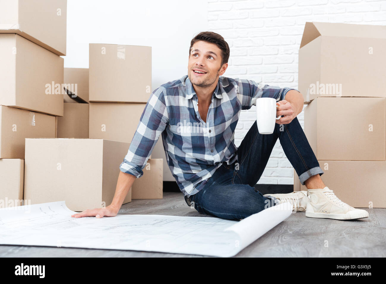 Handsome happy man looking at the house plan blueprint and holding cup ...