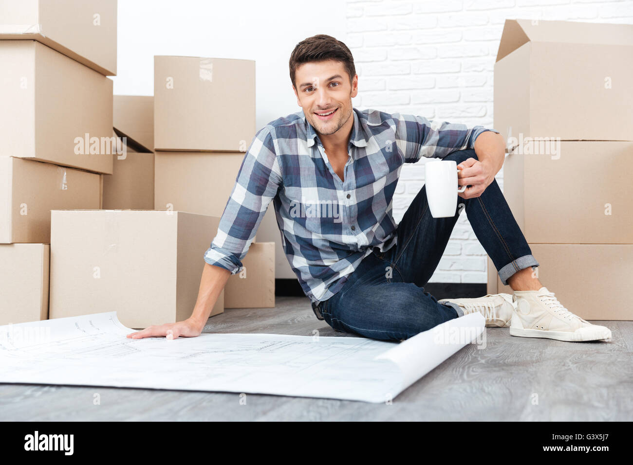 Happy young man looking at house blueprints and holding cup Stock Photo ...