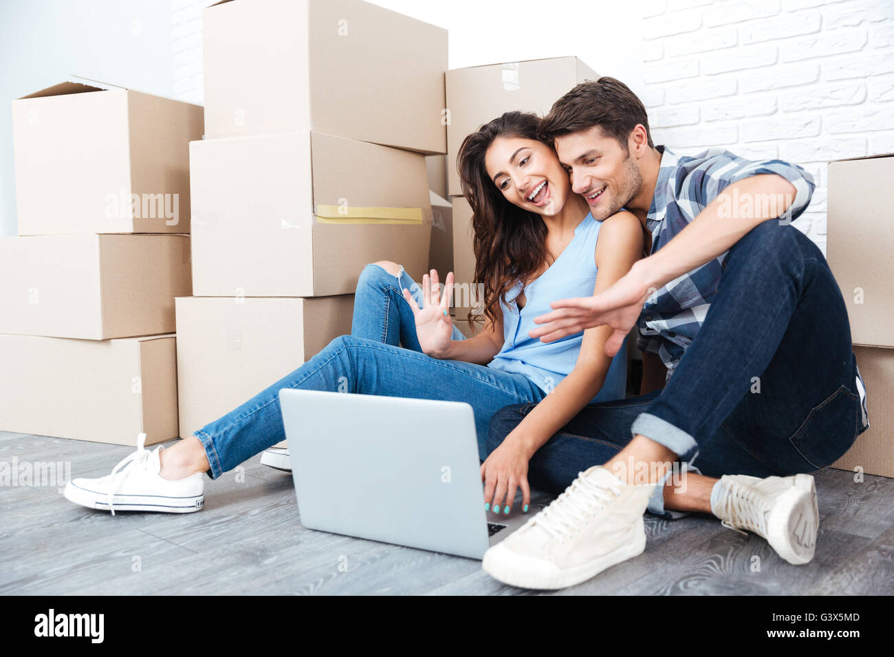 Young couple using laptop and showing keys to web camera while moving ...