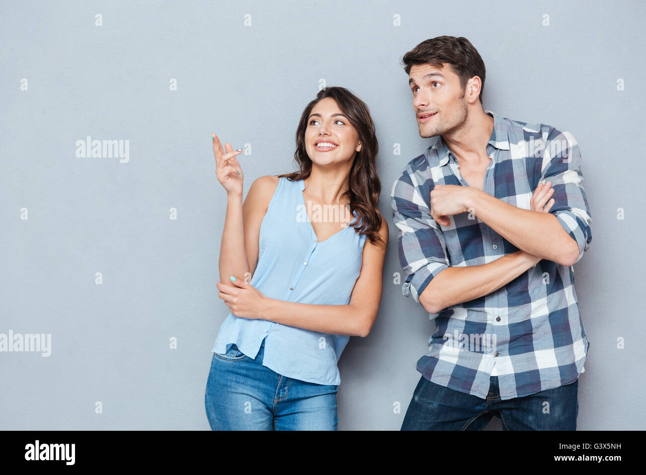 Attractive smiling couple standing and pointing at something on white ...