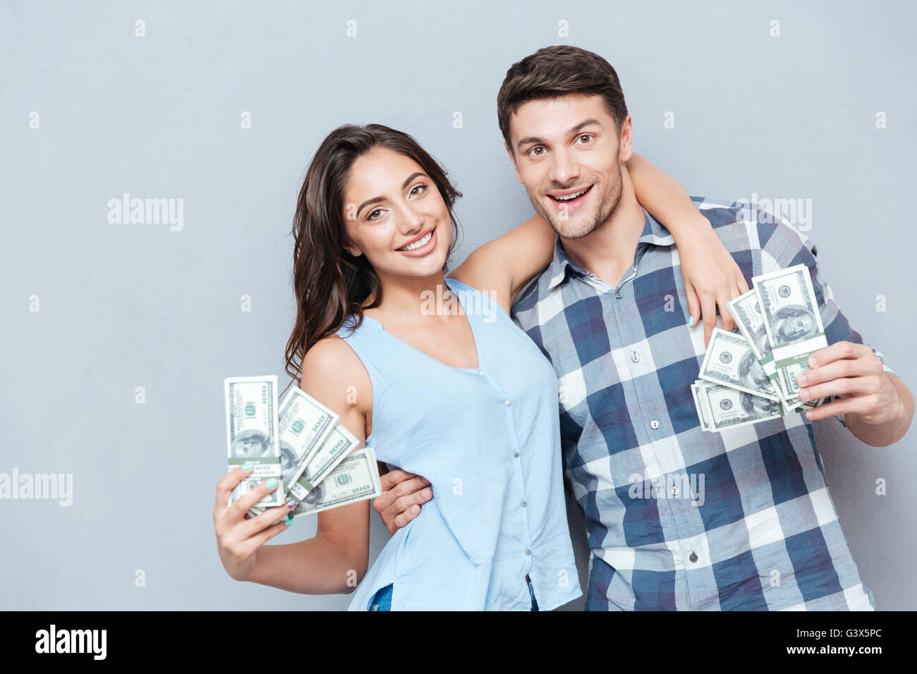 Happy young couple showing their money isolated on gray background ...