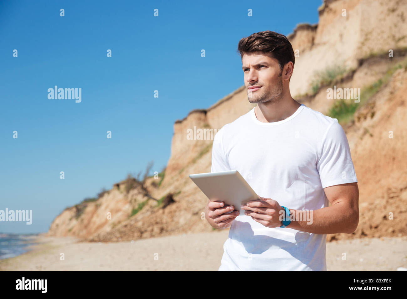 Pensive young man standing and using tablet on the beach Stock Photo ...