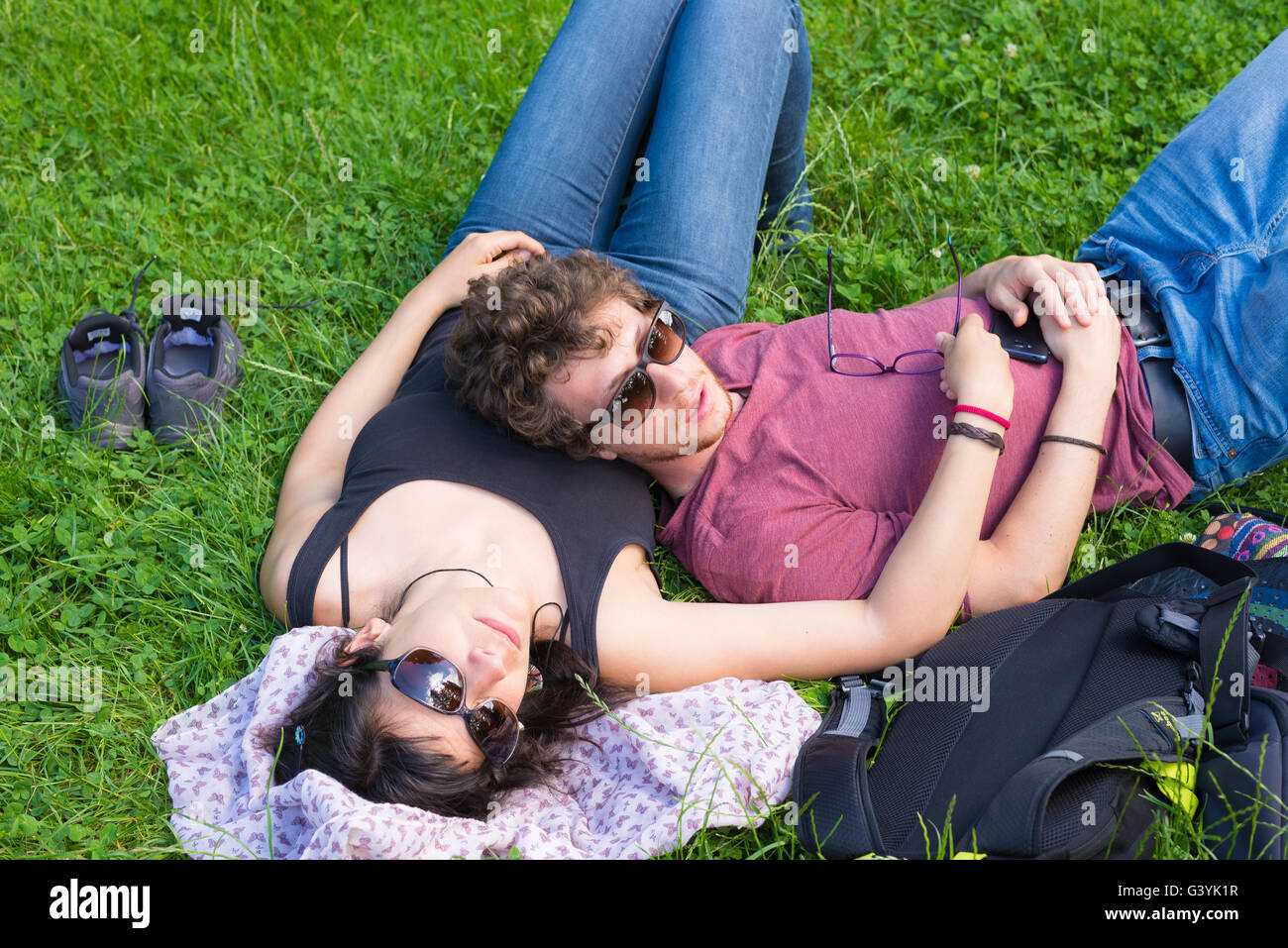 Young adult couple lying down on lush green grass in park, relaxing ...
