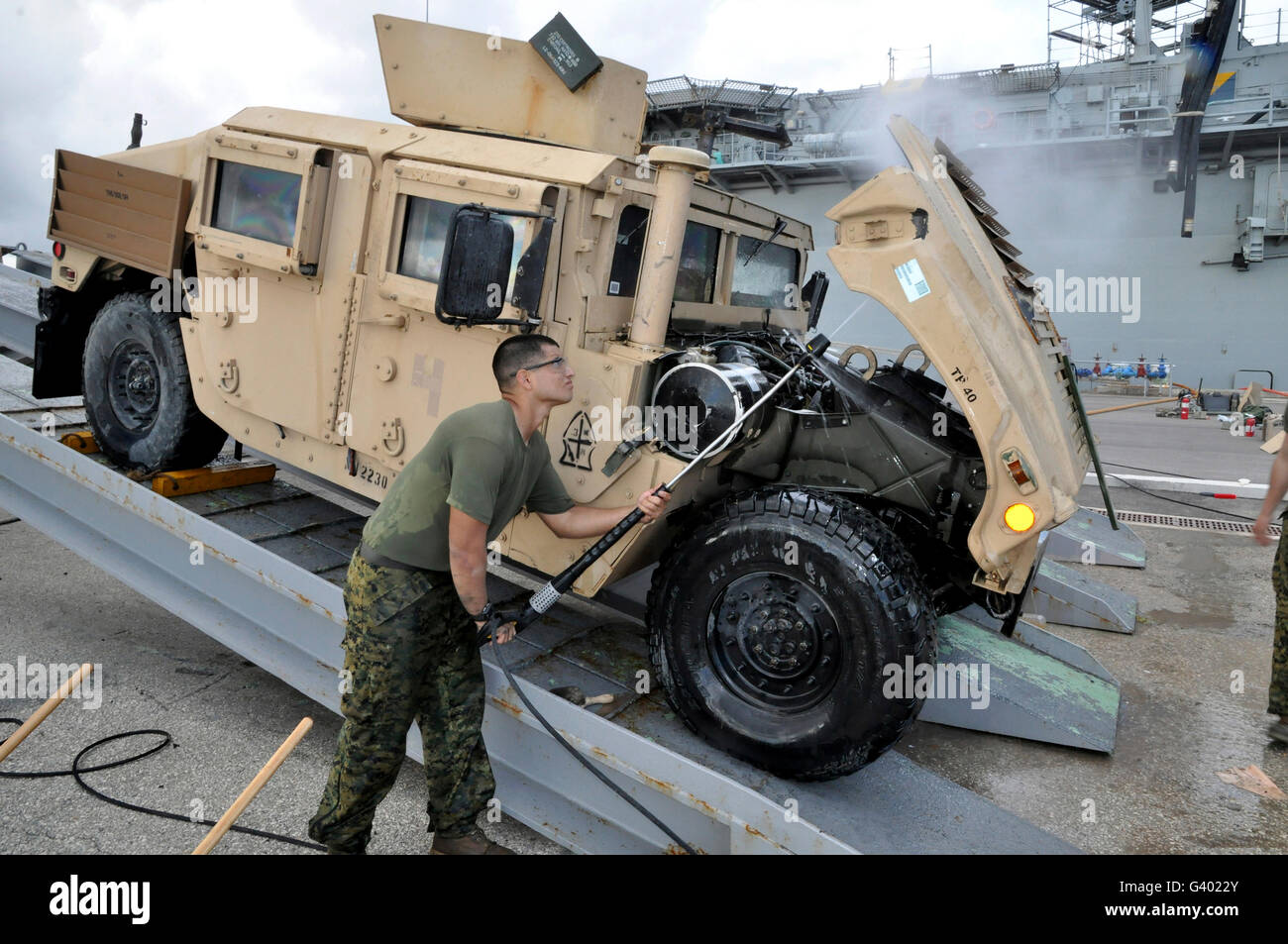 Marine uses a pressure washer to clean the underside of a Humvee hood ...