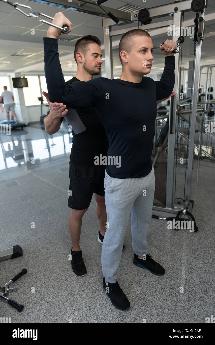 Personal Trainer Showing Young Man How To Train Biceps On Machine In ...