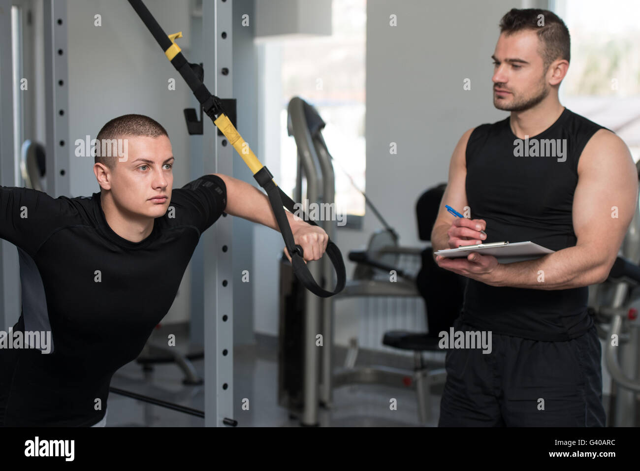 Personal Trainer Working With A Young Man At The Gym Writing Notes On A ...