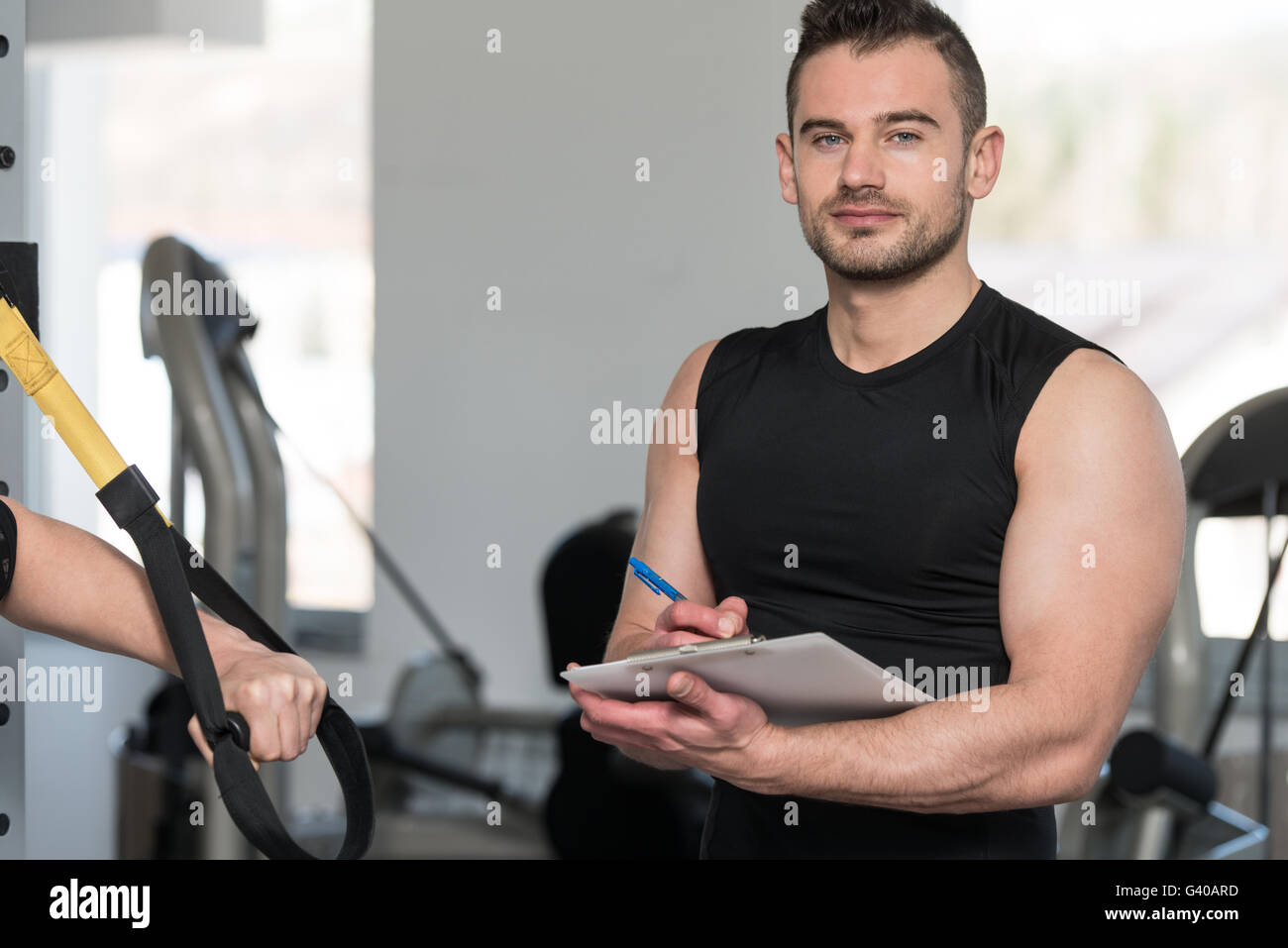 Personal Trainer Working With A Young Man At The Gym Writing Notes On A ...