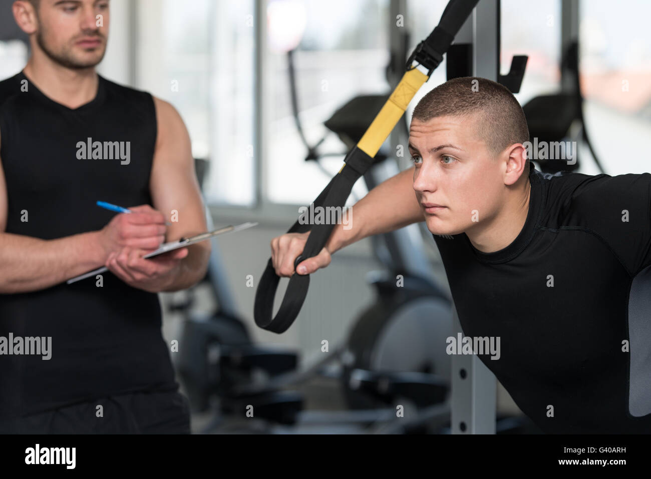Personal Trainer Working With A Young Man At The Gym Writing Notes On A ...