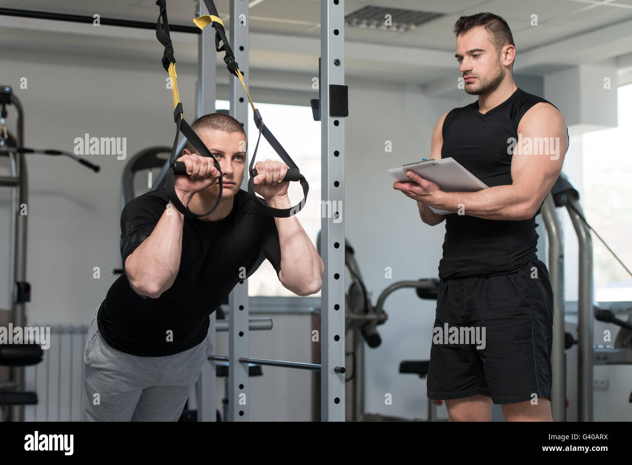 Personal Trainer Working With A Young Man At The Gym Writing Notes On A ...