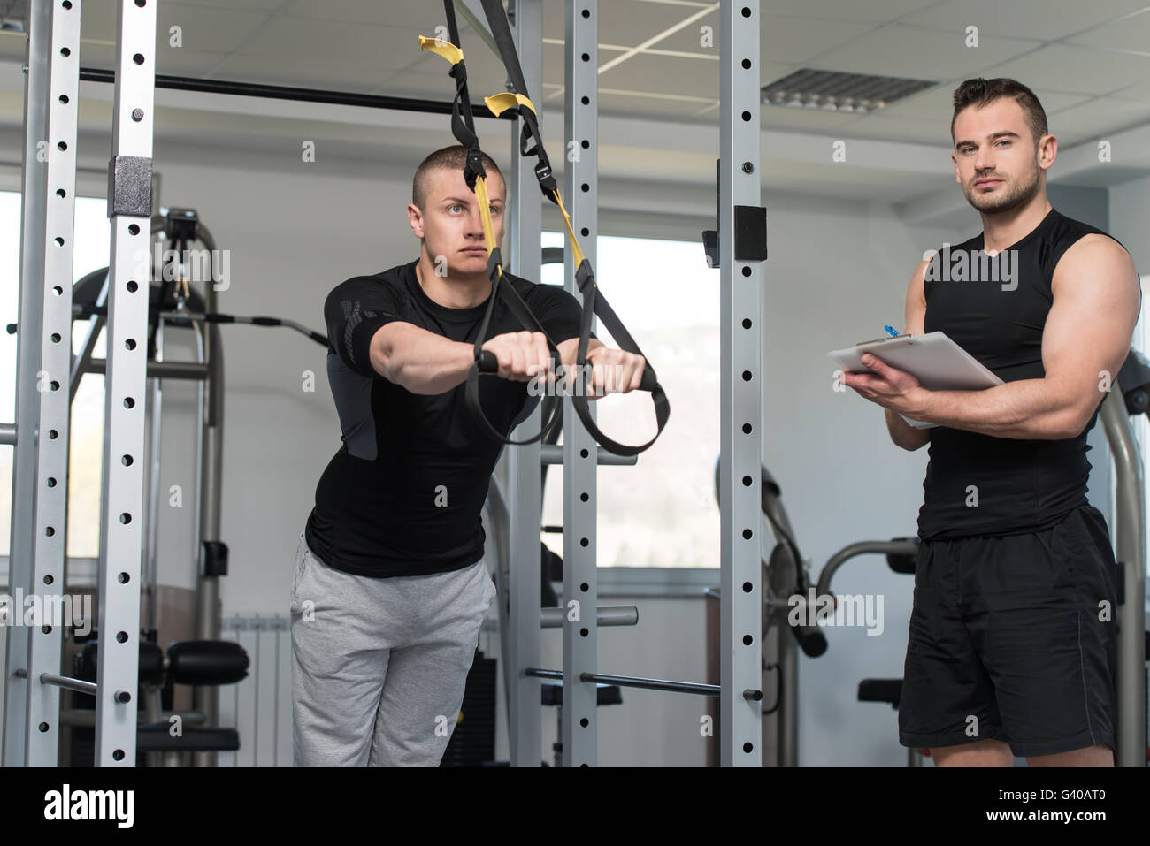 Personal Trainer Working With A Young Man At The Gym Writing Notes On A ...