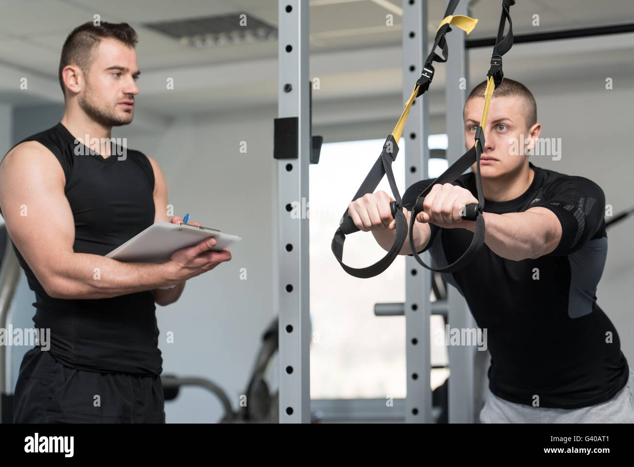 Personal Trainer Working With A Young Man At The Gym Writing Notes On A ...