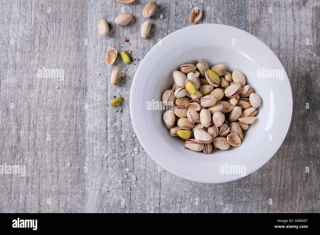 Salted roasted pistachios nuts with shell and salt in white ceramic plate over white wooden ...