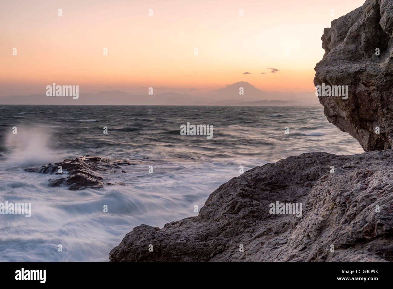 Strong waves crashing into sea rocks at sunset and Mount Fuji in the ...