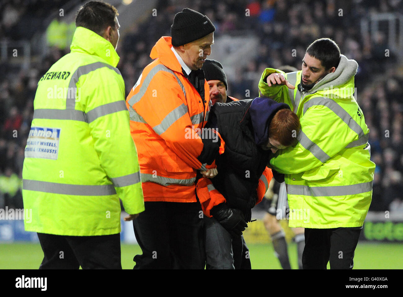 A pitch invader (centre right) is escorted out of the ground by ...