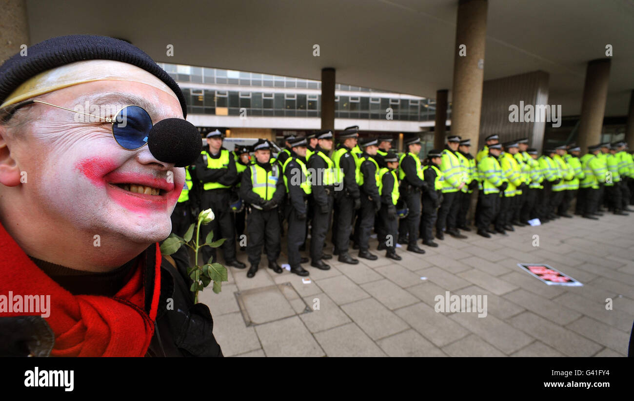 A lone protester dressed as a clown stands in front of a long line of ...