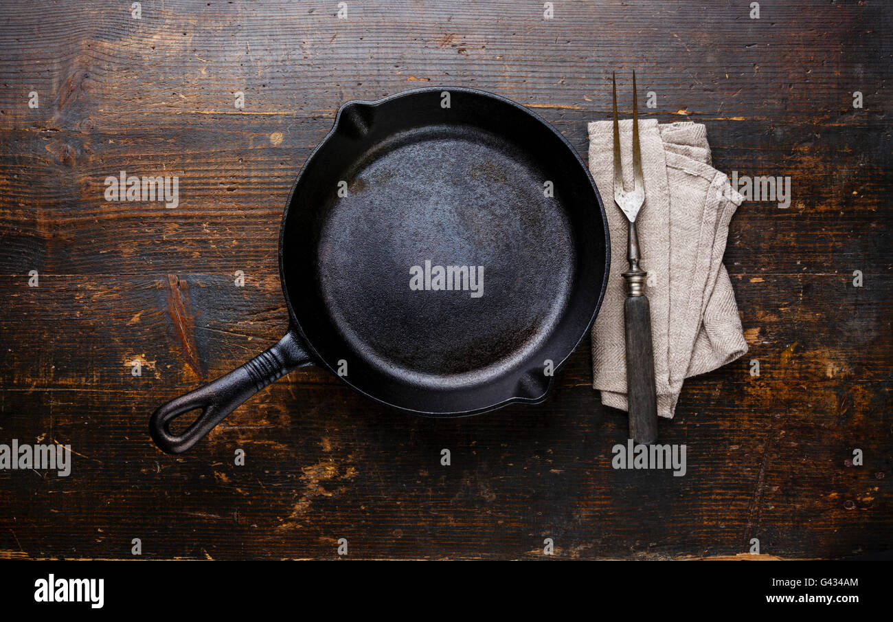 Black iron empty frying pan and meat fork on wooden texture background ...