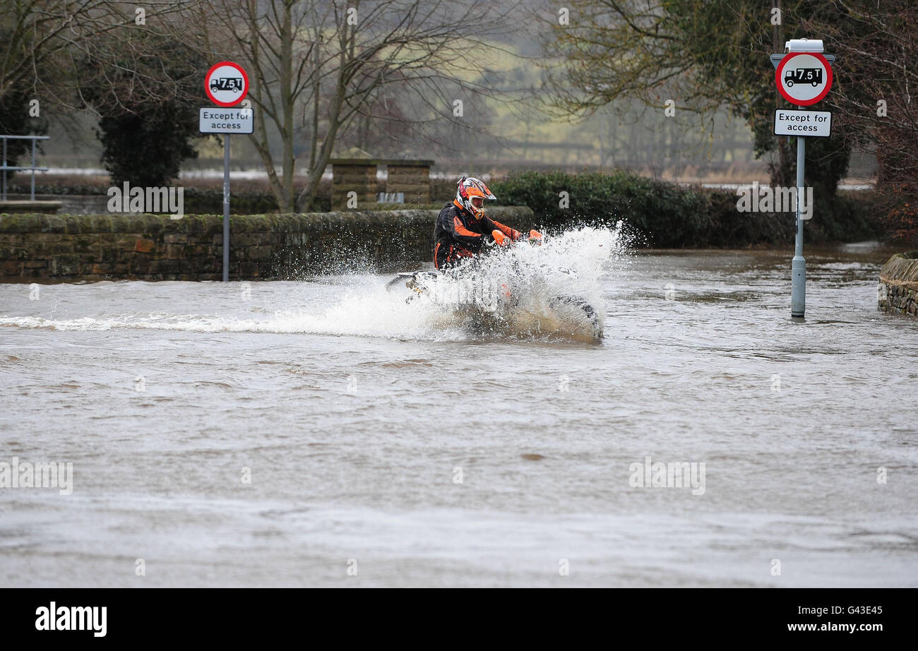 A motorcyclist rides through a flooded road at Darley Bridge near ...