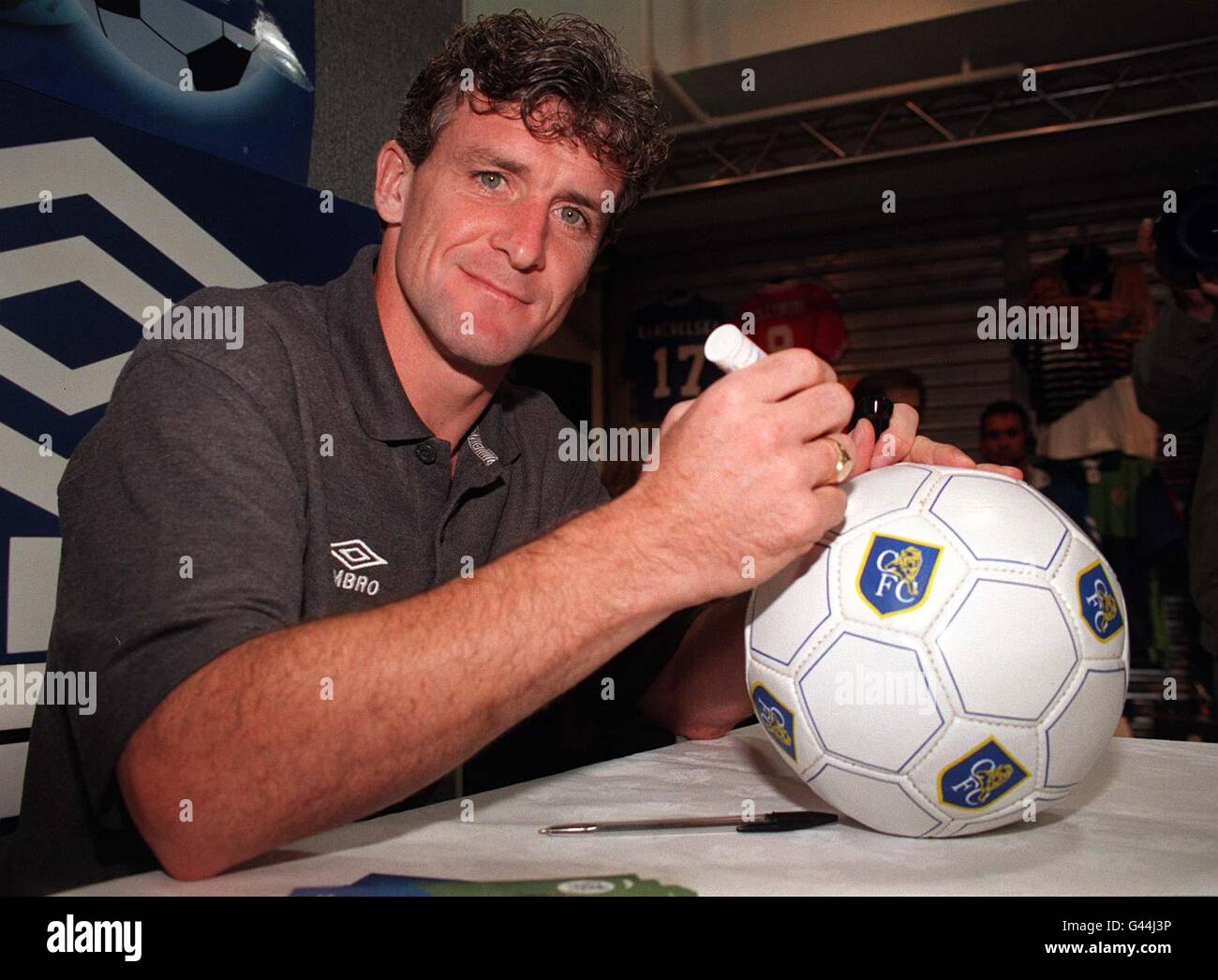 Chelsea striker Mark Hughes signing a soccer ball at the opening of the ...