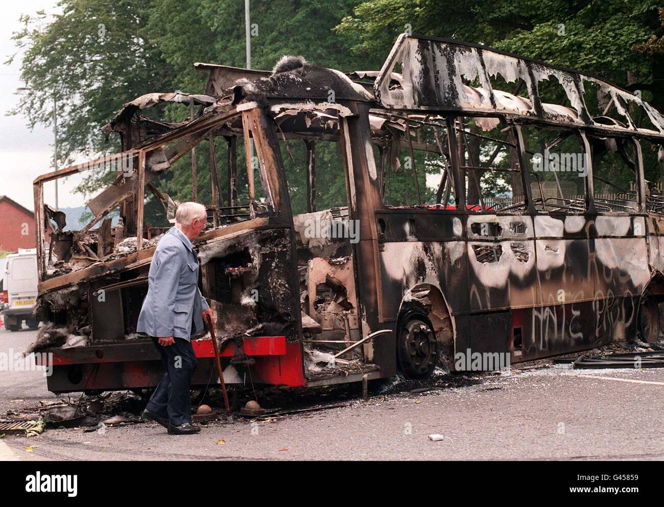 An elderly Belfast resident walks past a burned out bus on the ...