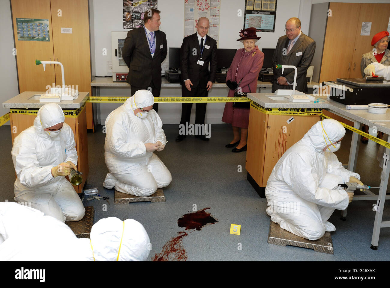 Queen Elizabeth II watches students as they examine a mock murder scene ...