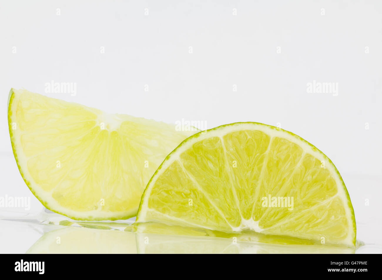 High key photo with wedges of lemon and juice on reflective surface ...