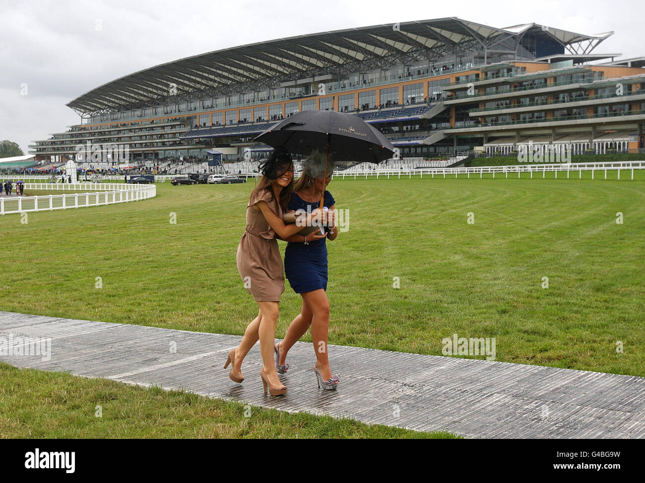 Female racegoers make their way around the course as the rain falls on ...